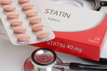 A close-up of a box labeled "Statin Tablets 40 mg" with a blister pack of round pink tablets, a stethoscope, and part of a prescription pad in the background.